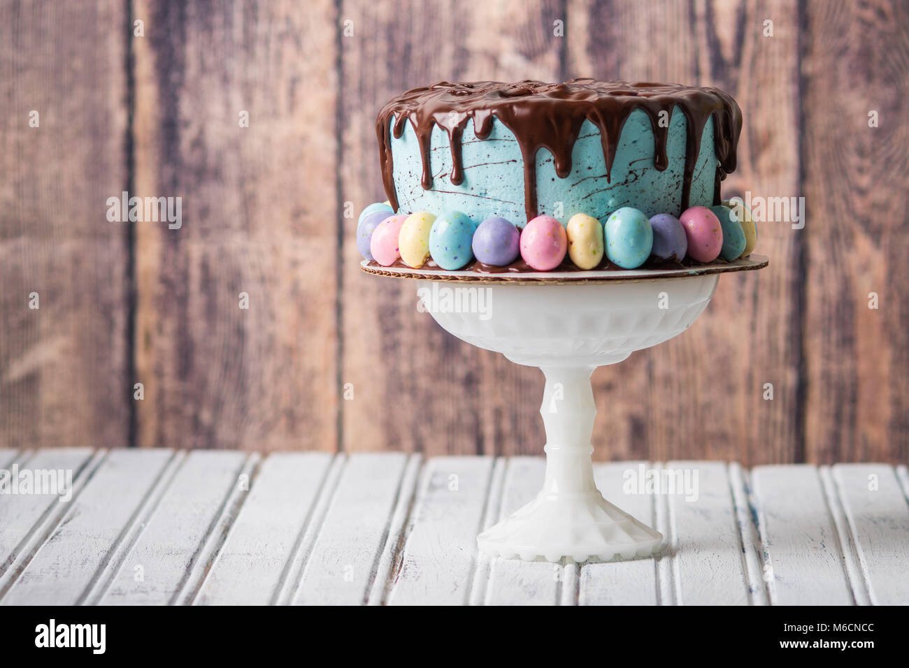 Blue frosted cake with chocolate drip frosting and Easter eggs in a ...