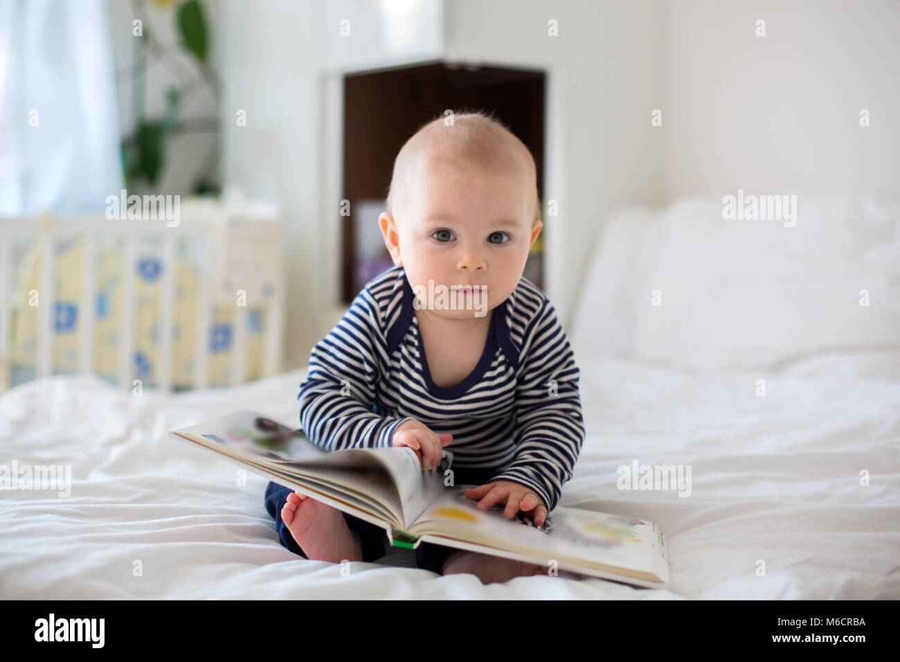 Portrait of a cute smiling infant baby boy reading a book. Happy ...