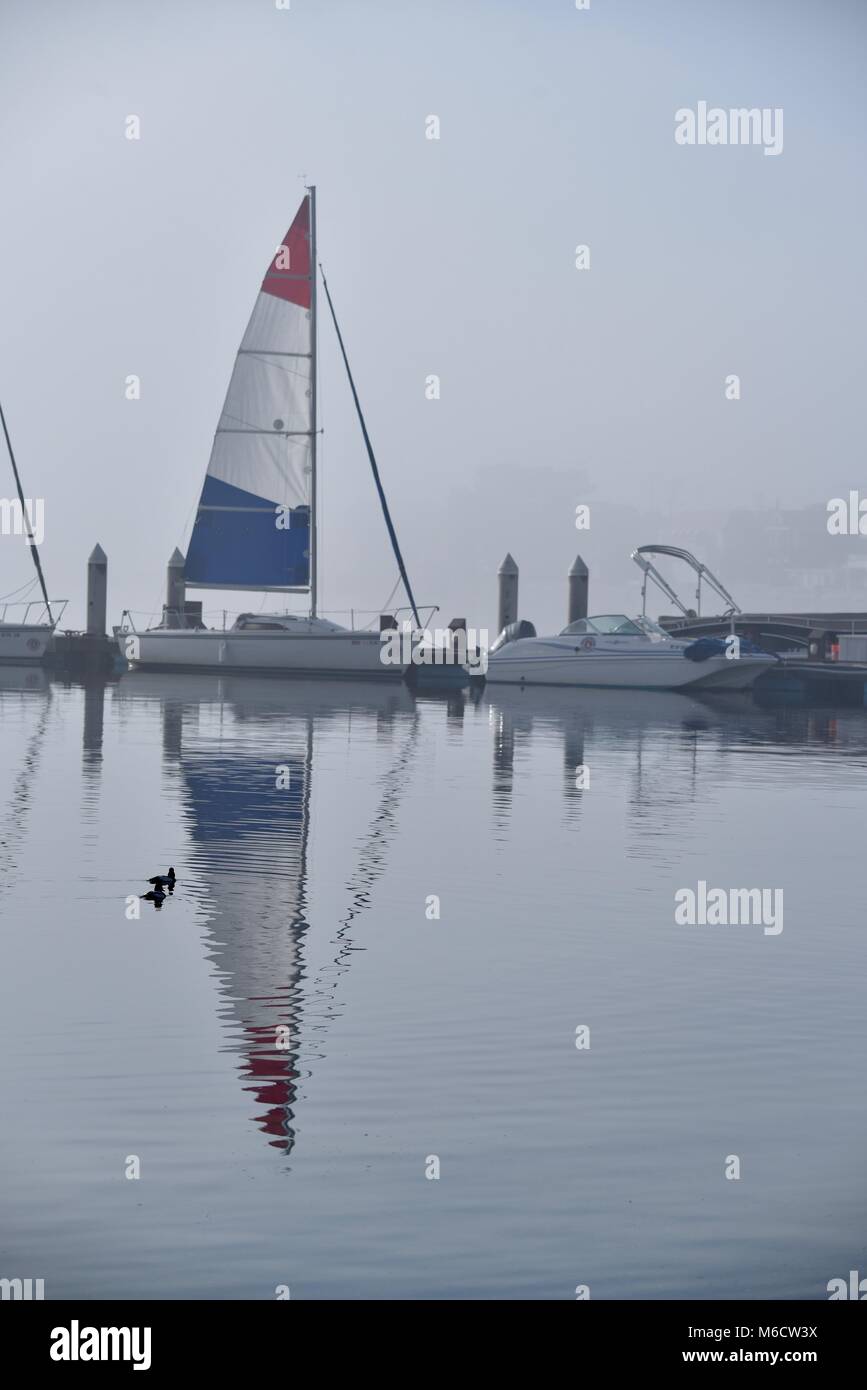 Sailboat with red, white and blue main sail up, tied up at dock, with ...