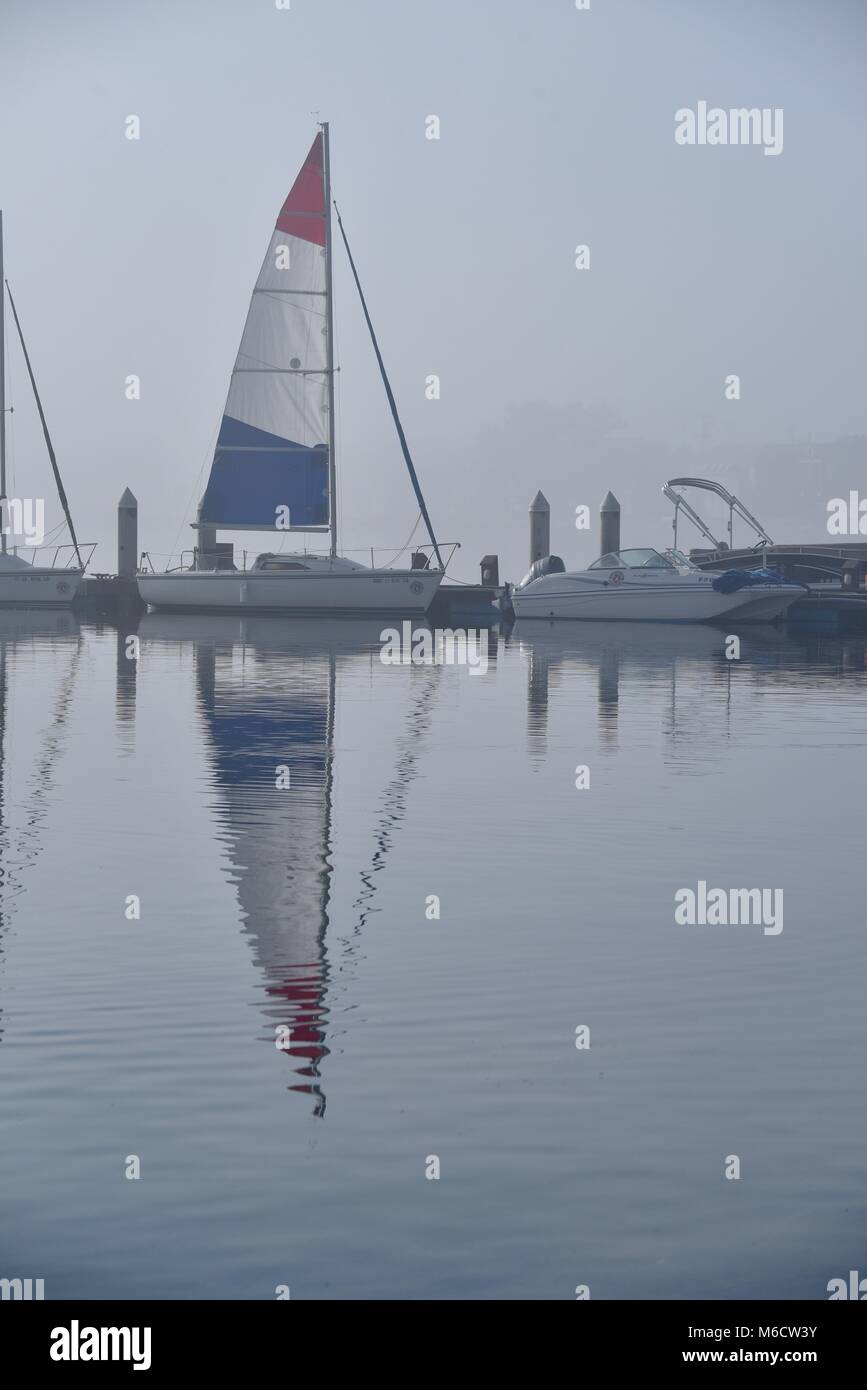 Sailboat with red, white and blue main sail up, tied up at dock, with ...