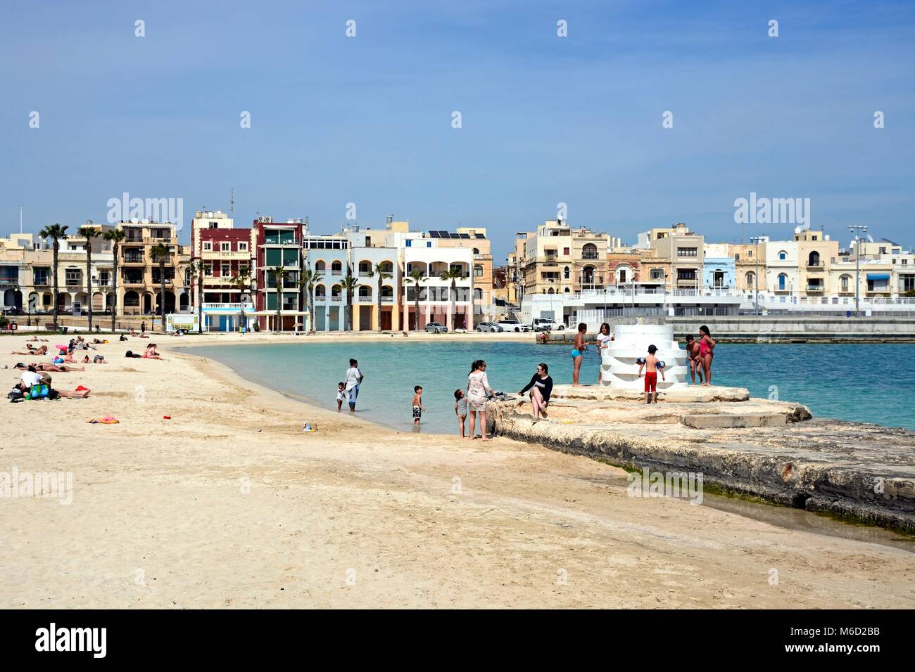 Tourists relaxing on the beach with waterfront buildings to the rear ...