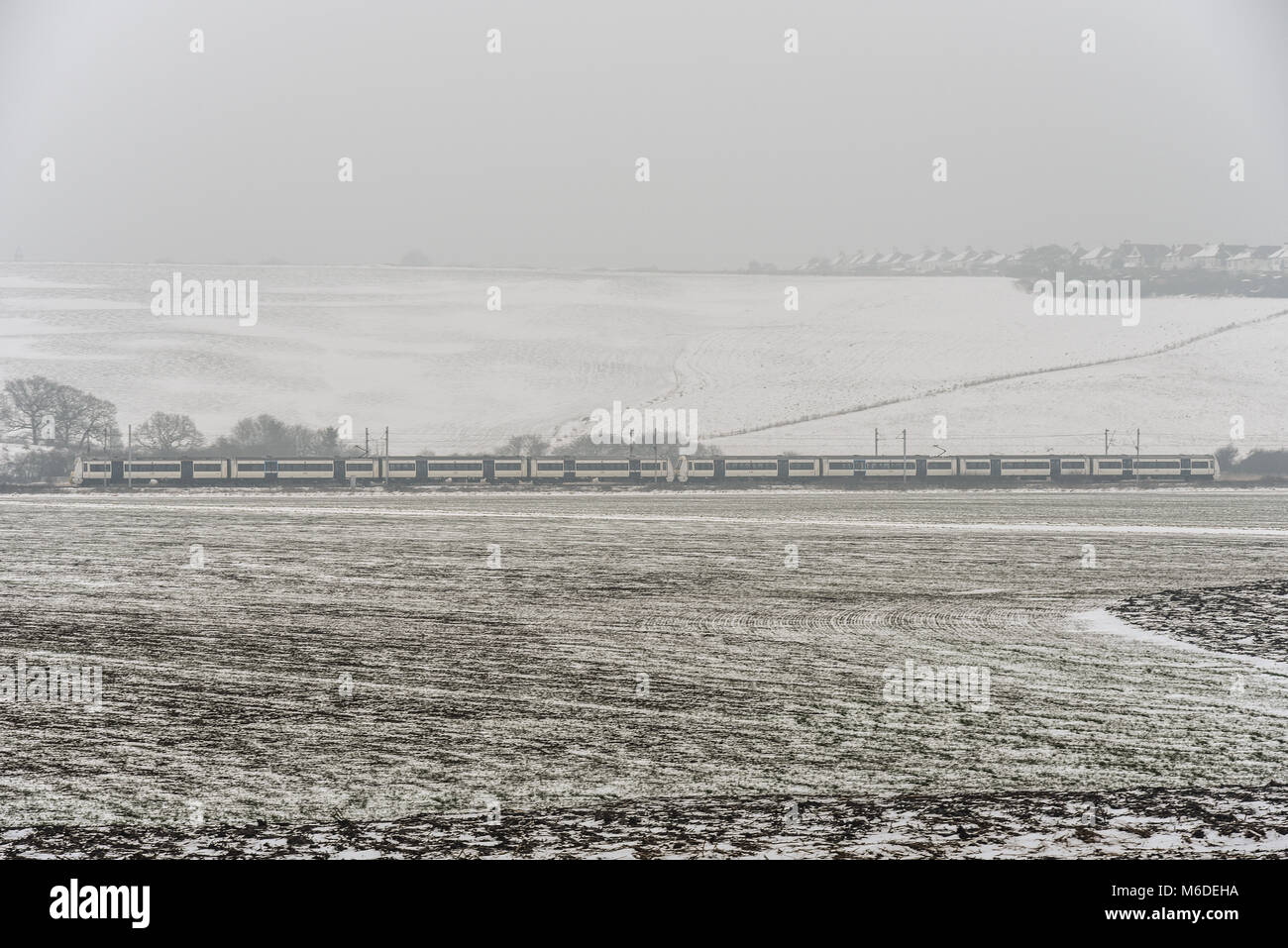 C2C railway train passing through snow covered Hadleigh Country Park ...