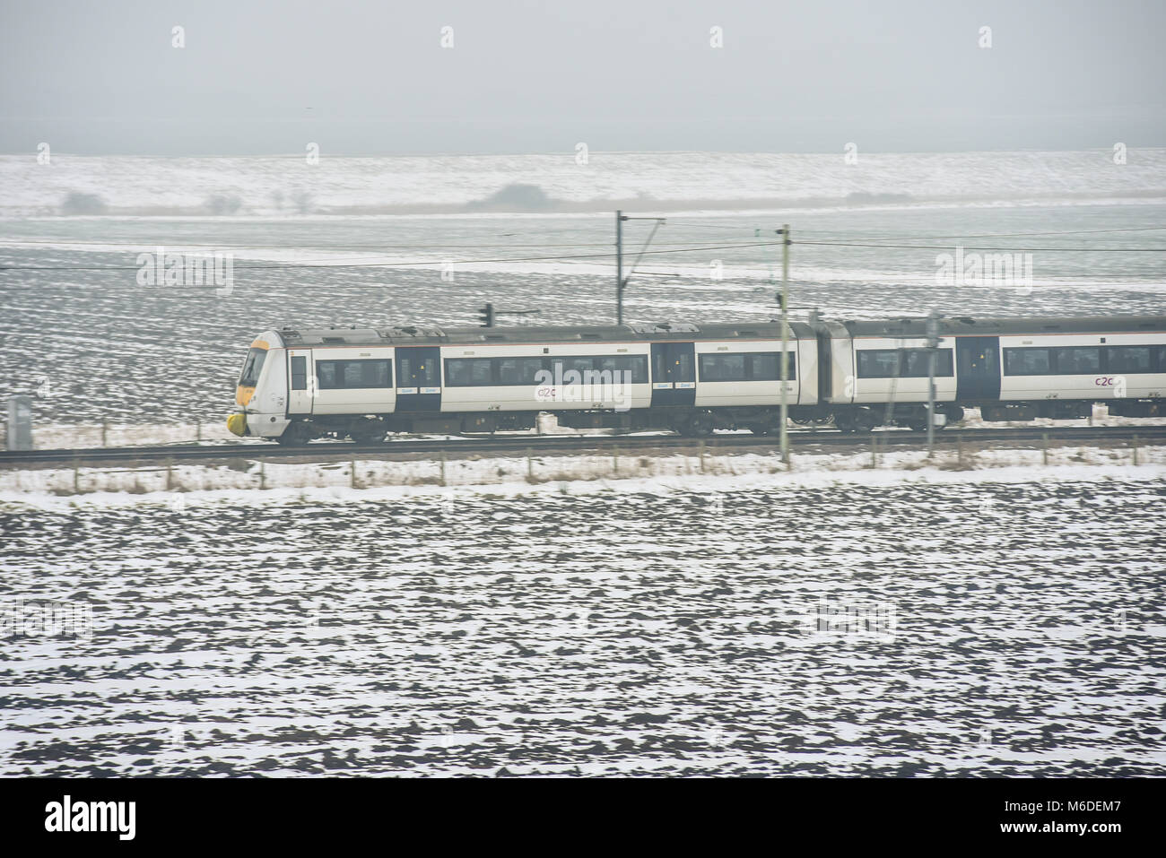 C2C railway train passing through snow covered Hadleigh Country Park ...