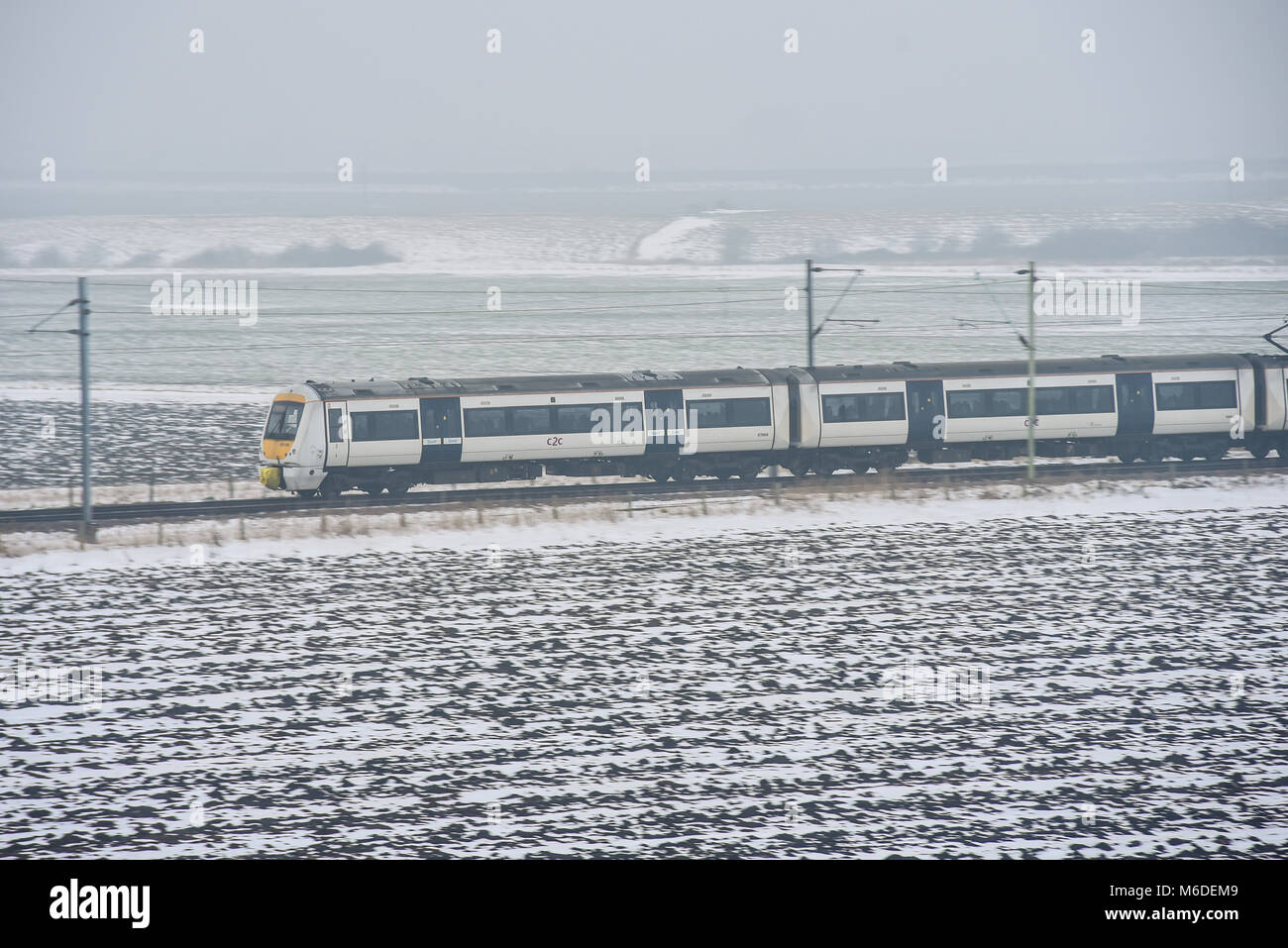 C2C railway train passing through snow covered Hadleigh Country Park ...