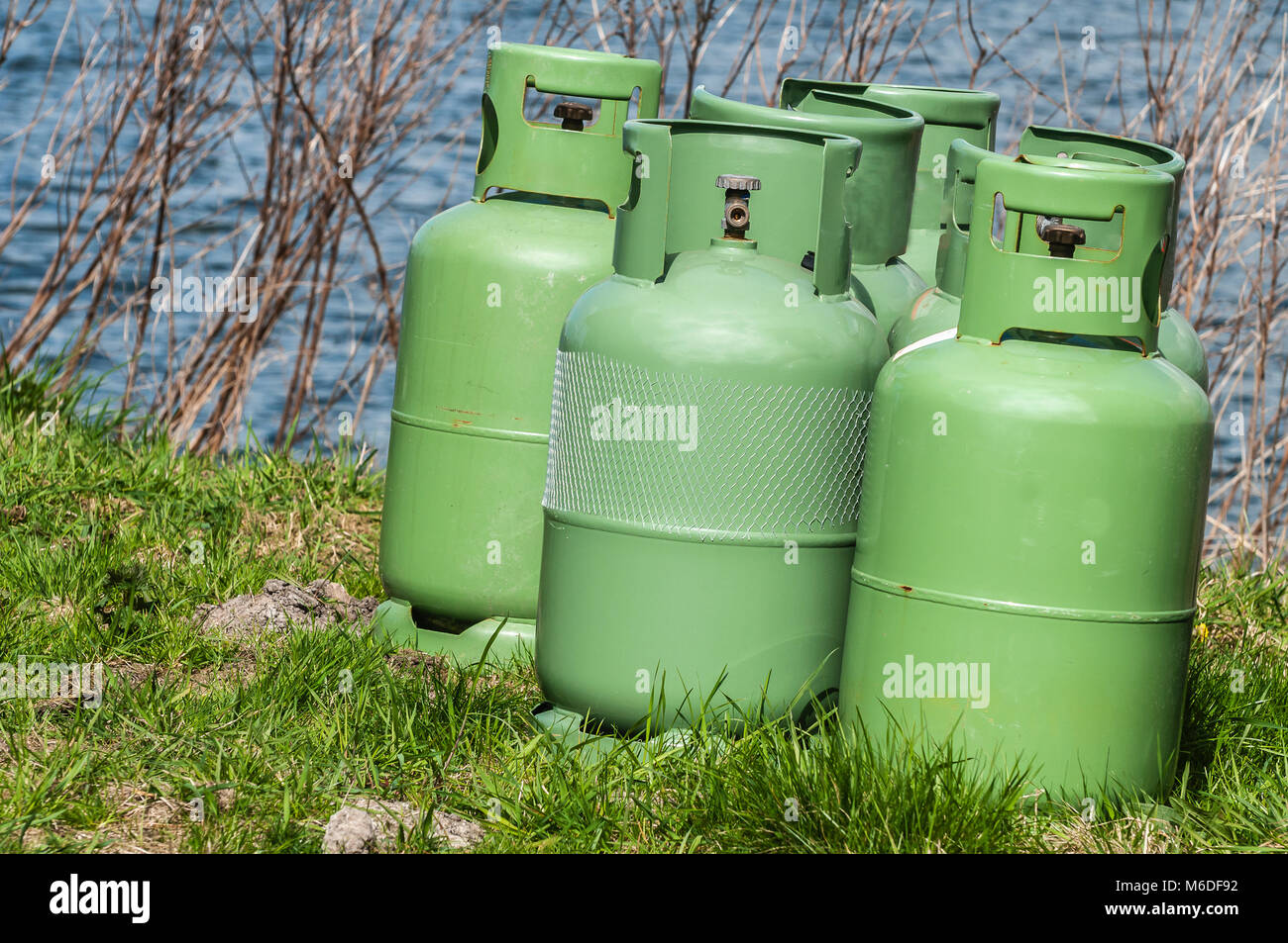 four propane storage bottles standing on a field near the water Stock ...