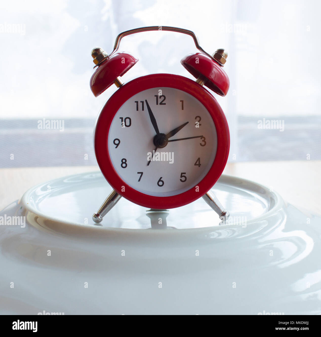 Red alarm clock on the plate. In the background is a window with ...