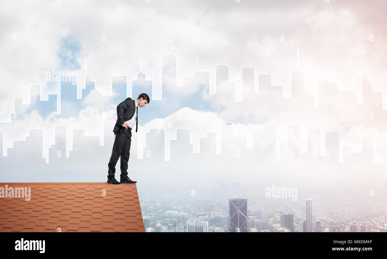 Businessman looking down from roof and modern cityscape at background ...