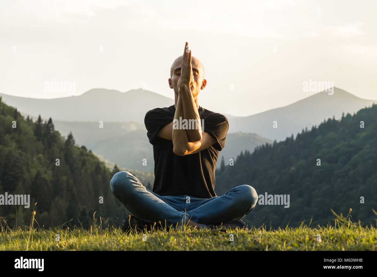 skinny male person peacefully sits in lotus position top of the hill in ...