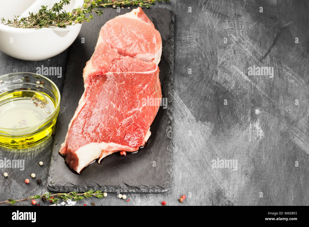Piece of raw meat of beef on a slate board with pepper and a thyme on a ...