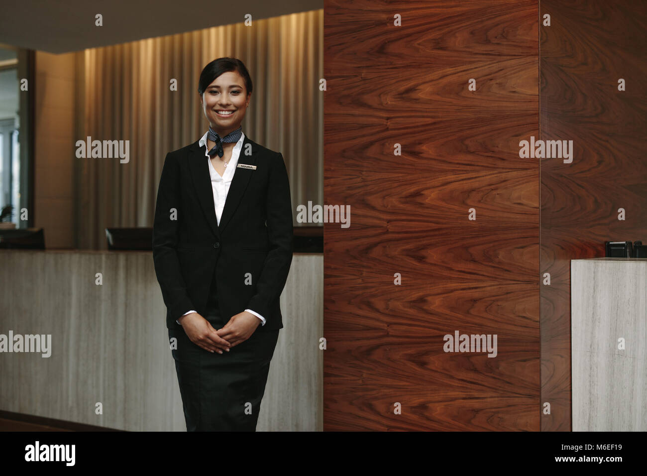 Portrait of happy young female receptionist standing at hotel front ...
