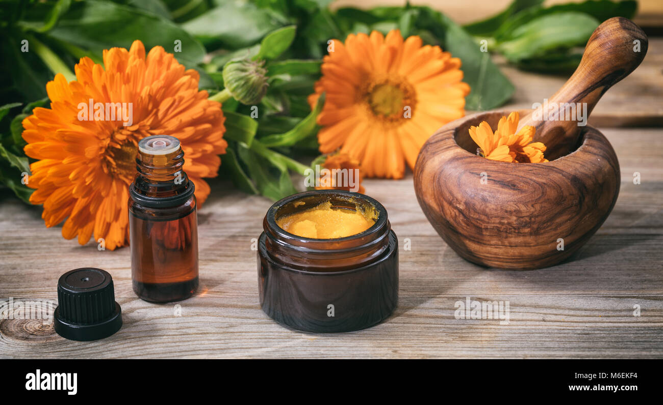 Calendula products. Essential oil, ointment and a mortar on a wooden ...