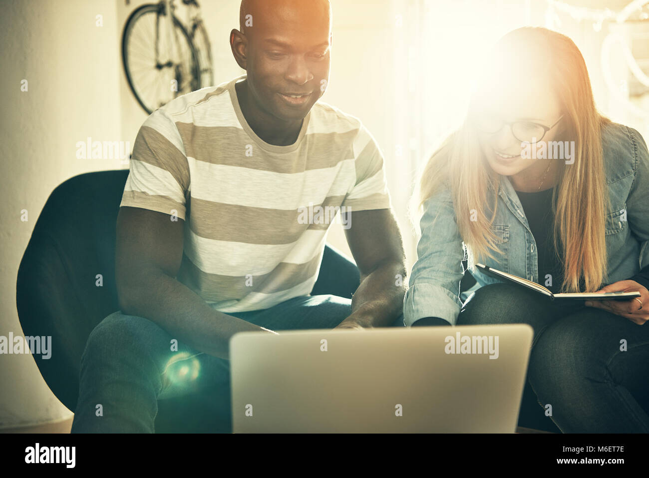 Two diverse colleagues smiling while sitting together working on a ...