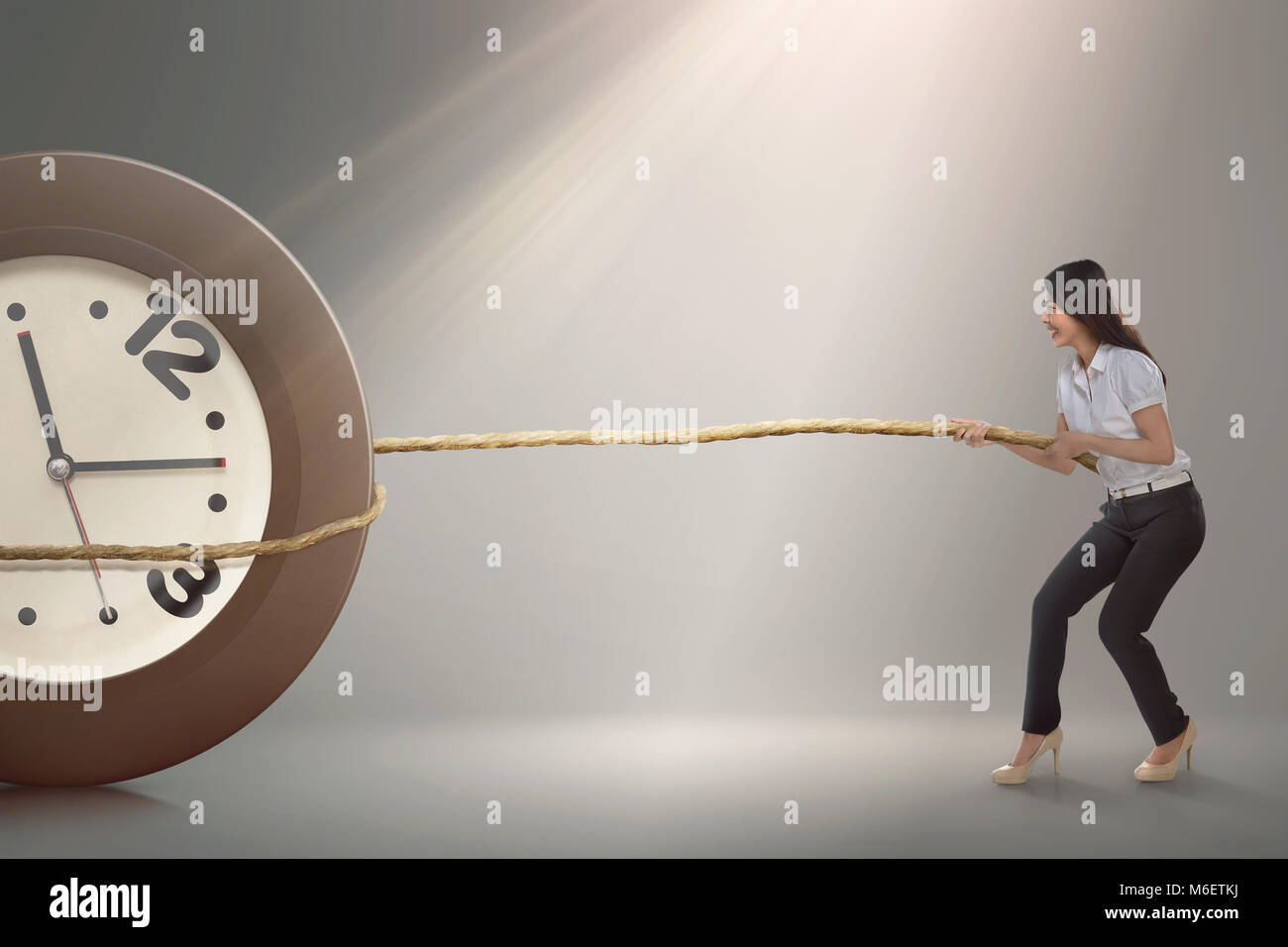 Pretty asian businesswoman pulling a clock with rope over gray ...