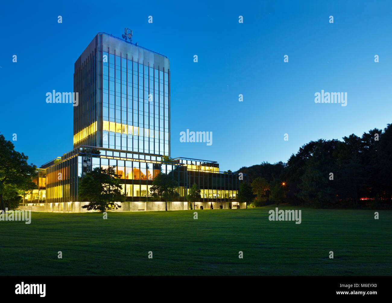 A steel and glass bank building surrounded by a park in the evening ...