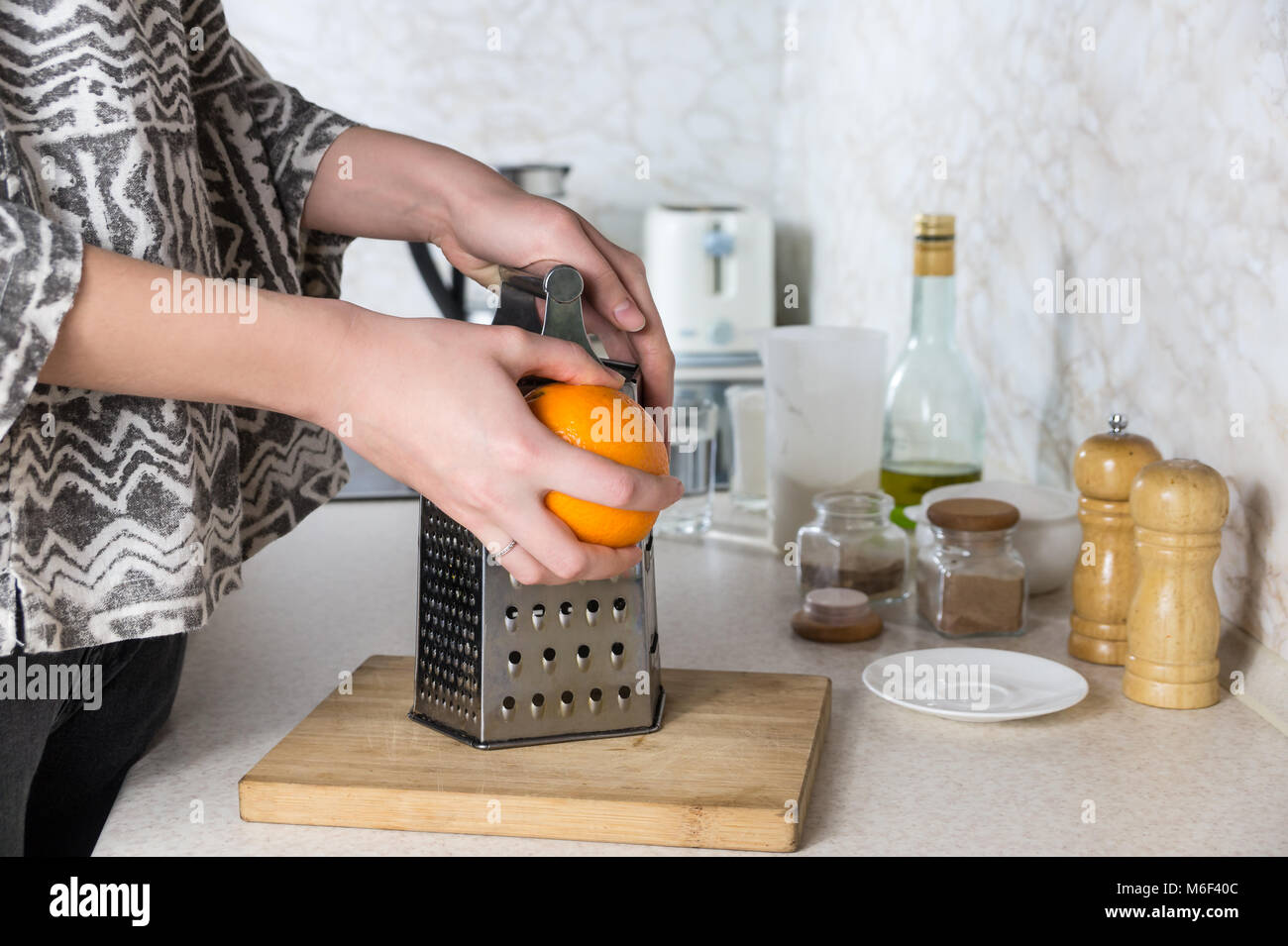 Grating orange zest. Female hands use grater to make peel in kitchen ...