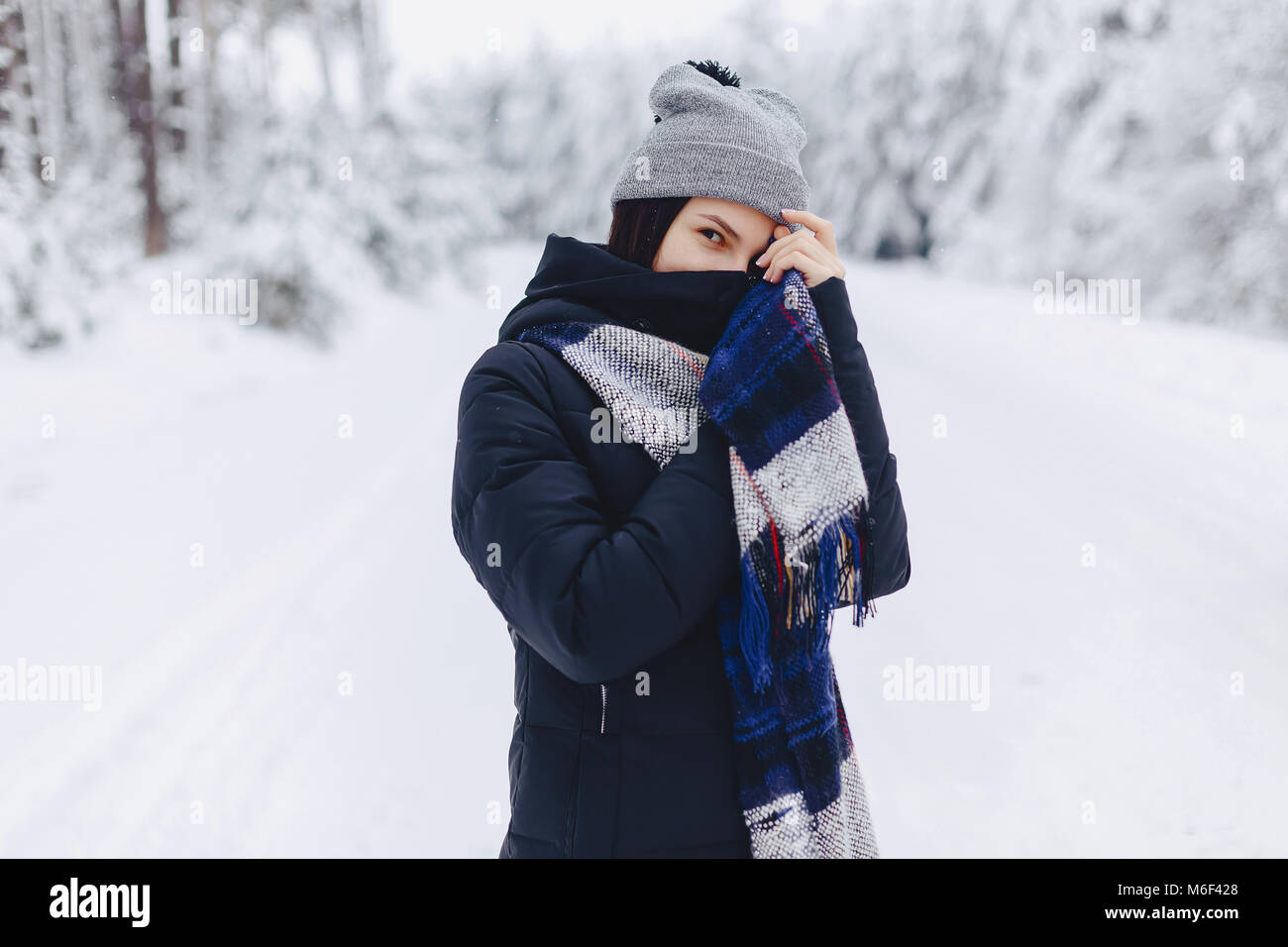 A girl wearing a winter hat poses on a camera in the background of ...