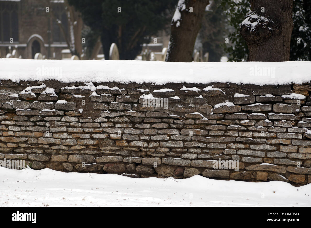 A snow-covered stone wall at All Saints Church churchyard, in ...
