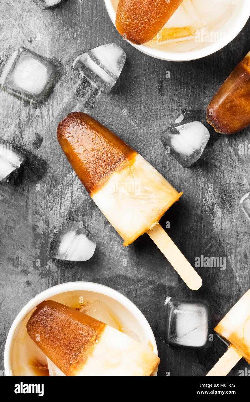 Coffee ice cream popsicles in white cups on a dark background. Top view ...