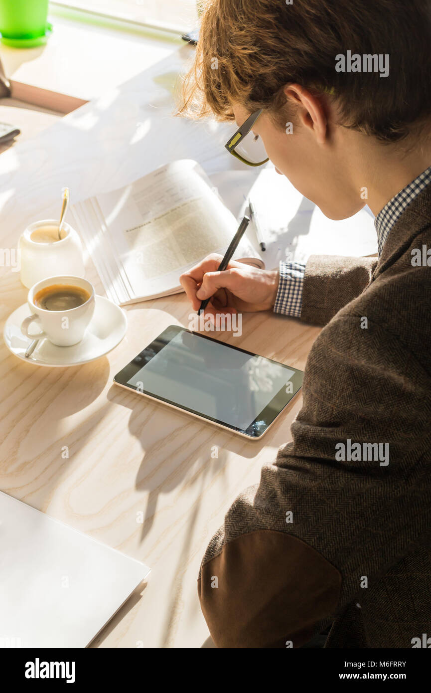 Handsome teenage person in reading eyeglasses works with tablet pc and ...