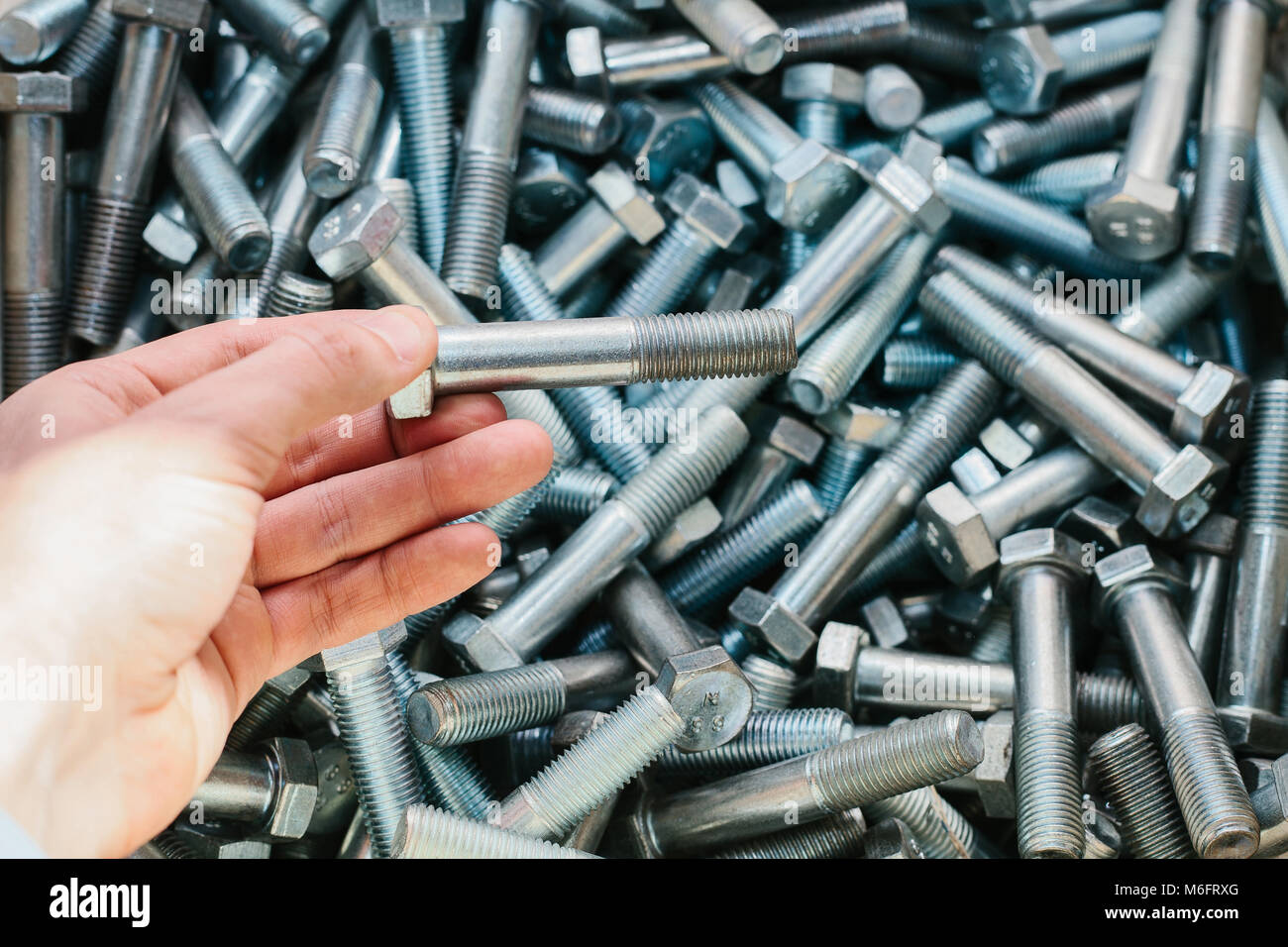 A man is holding a building bolt. Many different fastening tools used ...