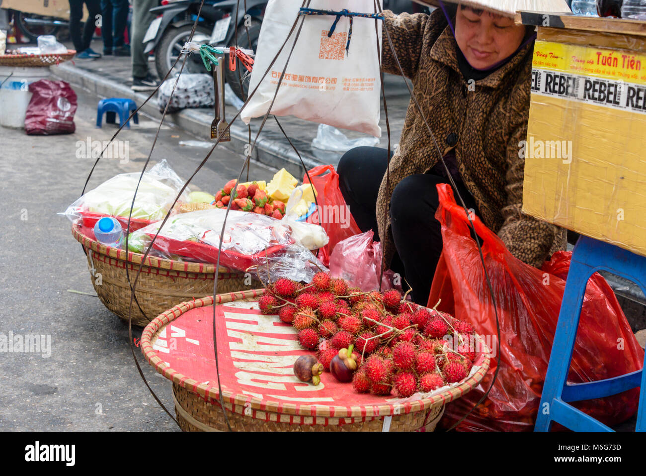 A woman carries fruit in baskets slung from her bamboo carrying pole in ...