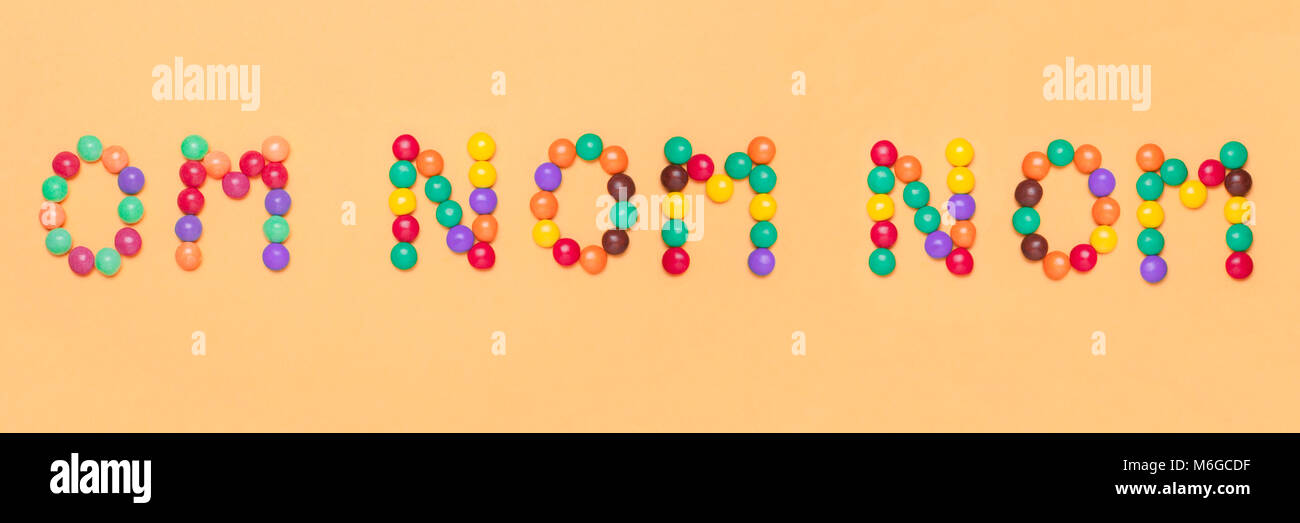 The word OM NOM NOM is written by sweet colorful chocolate candy on ...