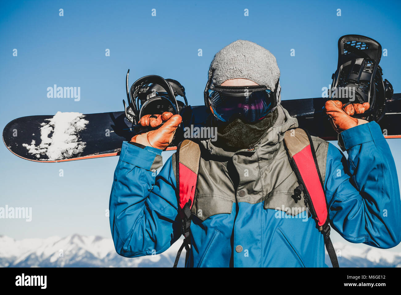 Enthusiastic snowboarder holding his snowboard on his shoulders while ...