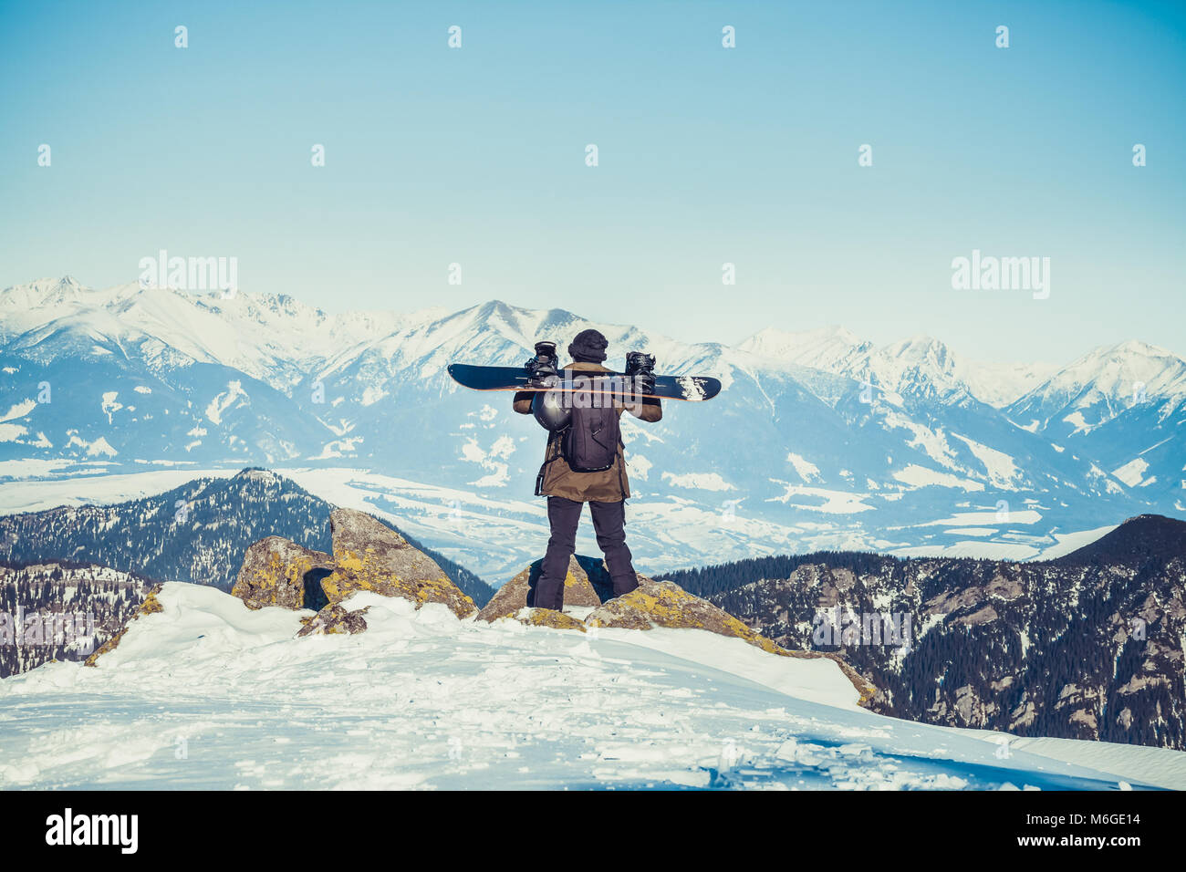 Snowboarder standing at the very top of a mountain, holding snowboard ...