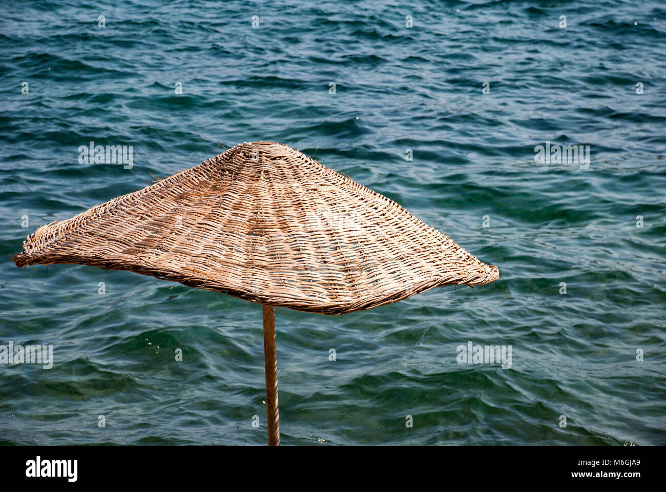 Straw beach umbrella against the vibrant backdrop of sea waves ...