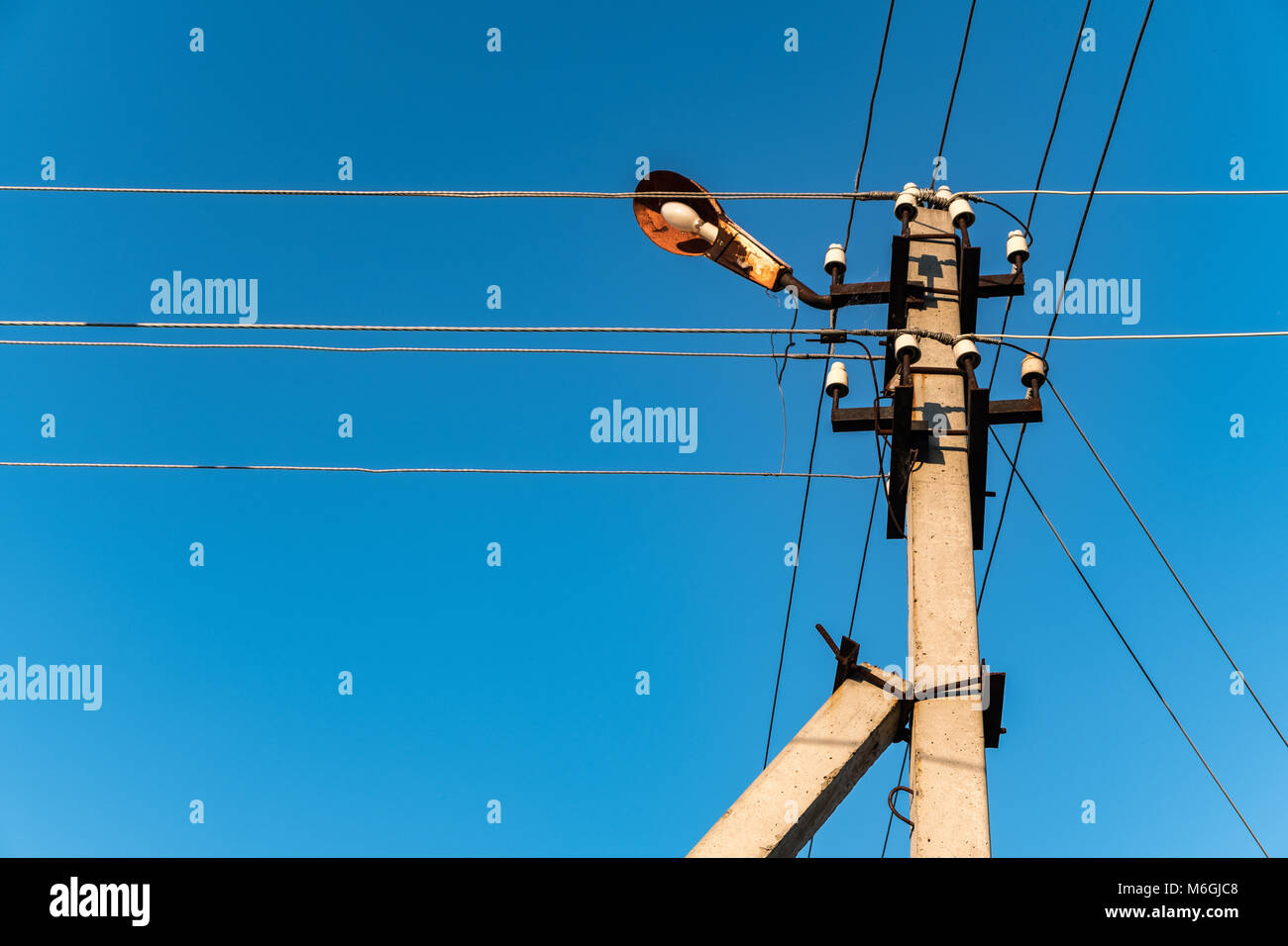Electric pole with lamp and intersecting wires on a background of blue ...