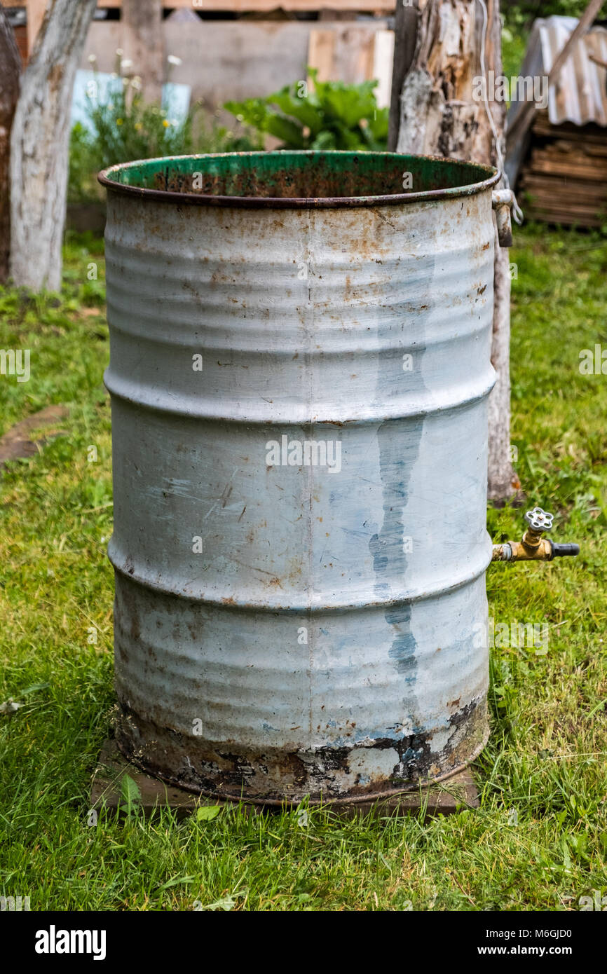 Old rusty rain barrel with a water tap standing on the green lawn of ...