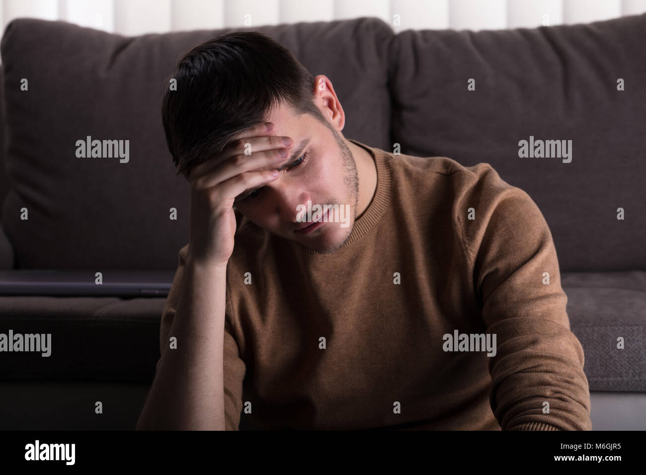 Young Sad Man Sitting In Front Of Sofa At Home Stock Photo - Alamy