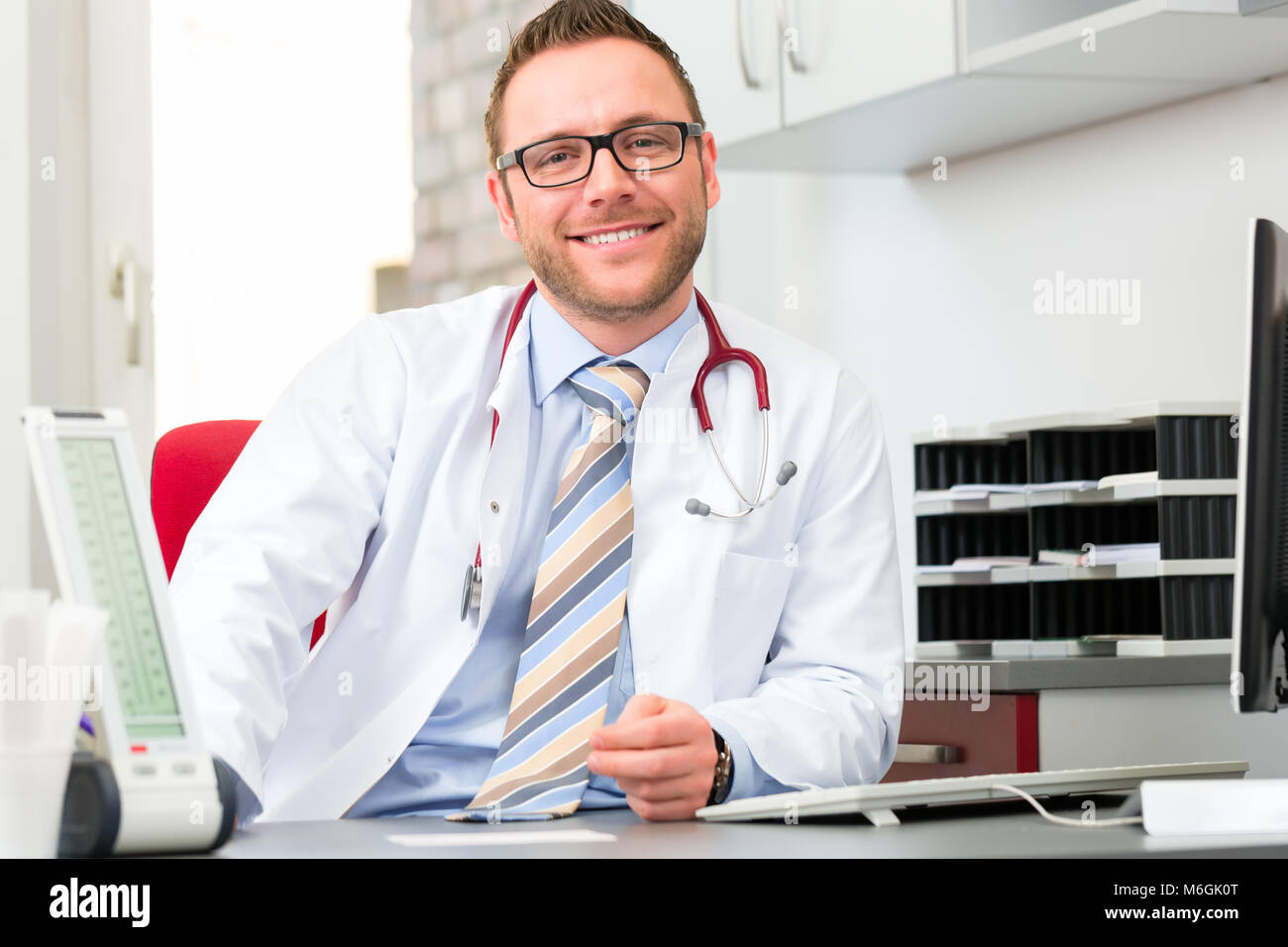 Young doctor sitting in surgery at desk Stock Photo - Alamy