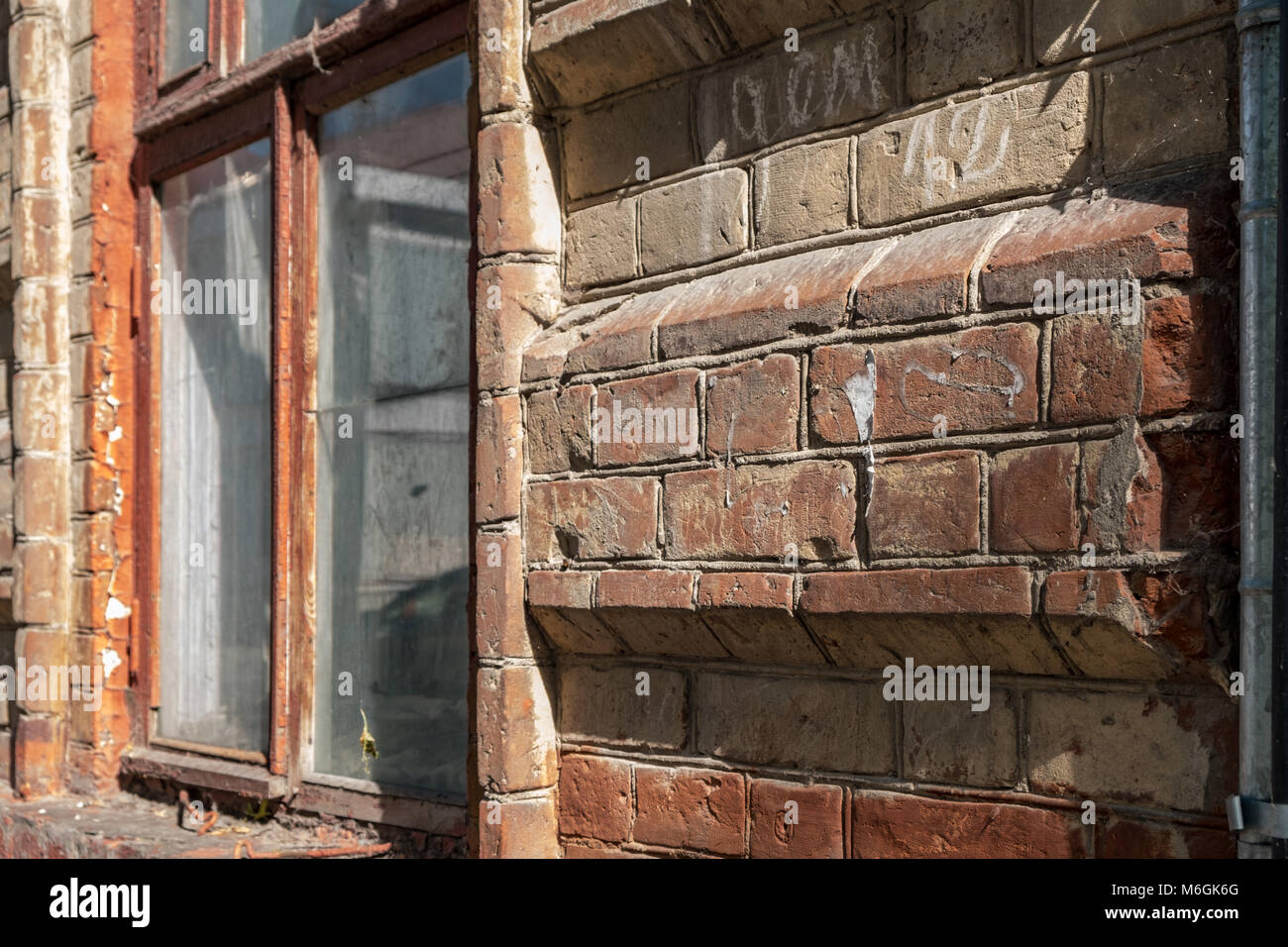 Vintage building's red brick wall with window framed in peeling red paint. Historical building ...