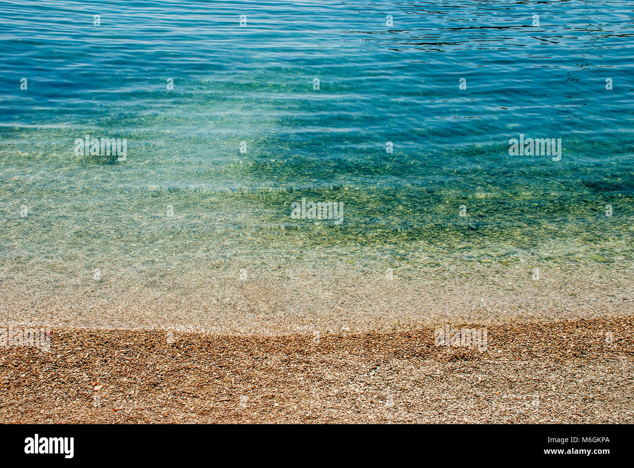 Crystal clear sea waters at a pebble beach with green seaweed. Omis ...
