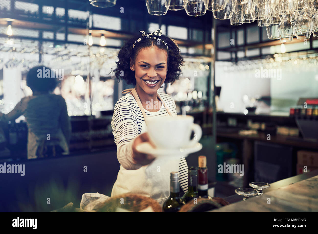 Young African barista smiling while standing behind the counter of a ...