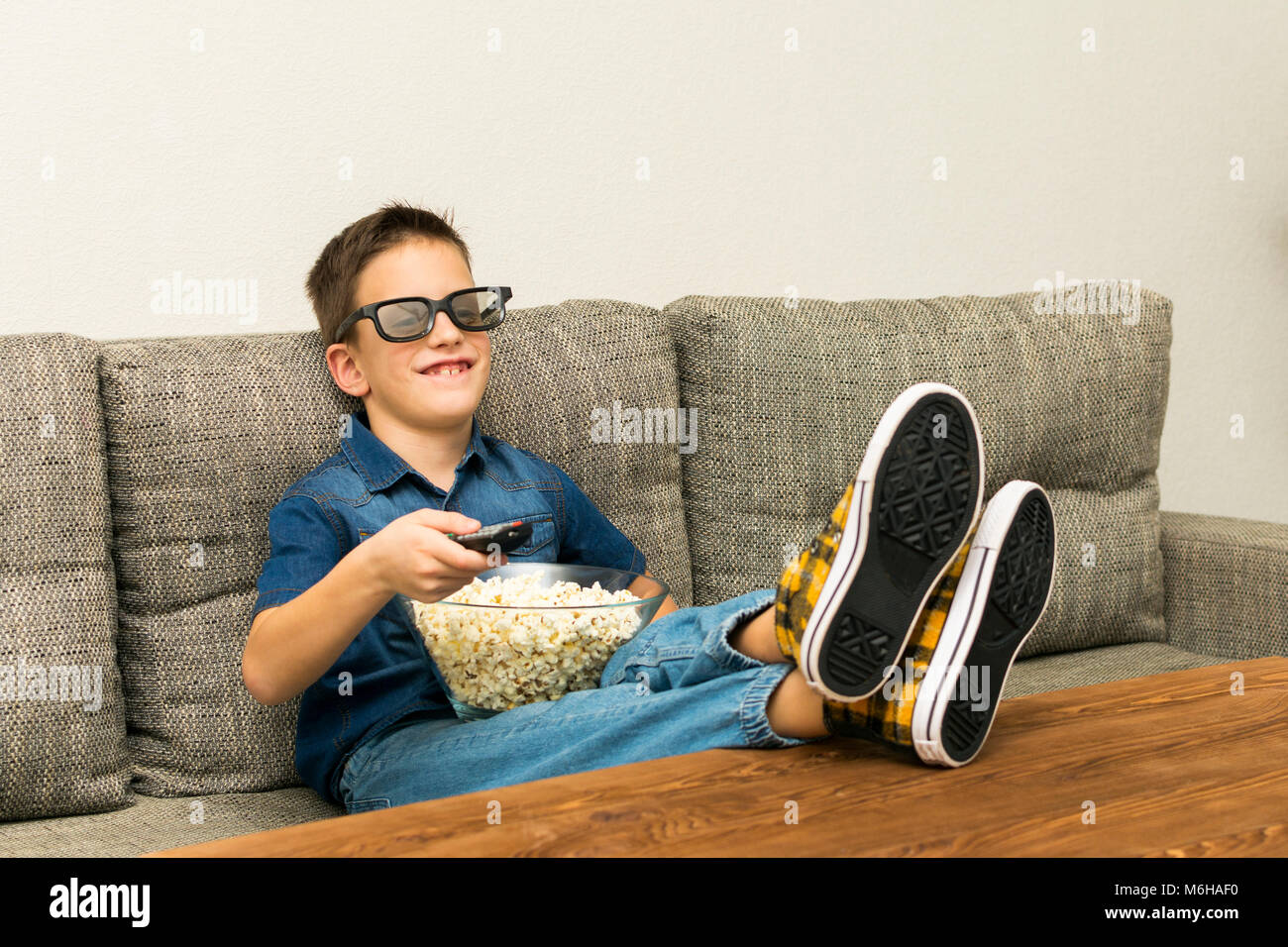 Small boy on the couch watching TV and eating popcorn. Legs on table ...