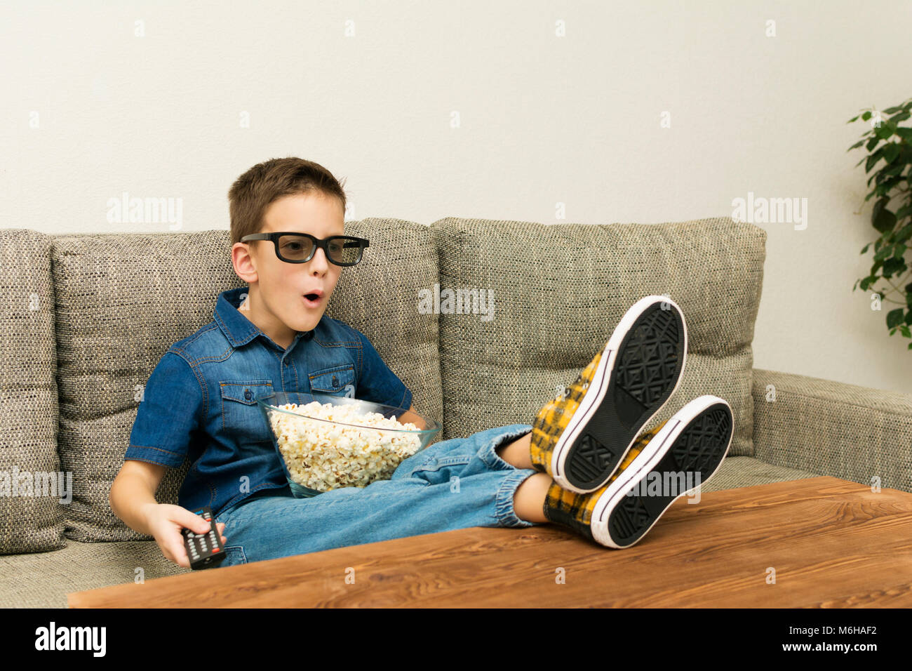 Small boy on the couch watching TV and eating popcorn. Legs on table ...