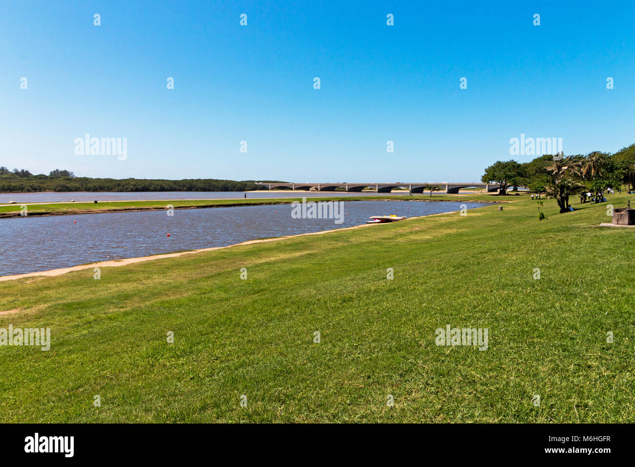 Green mowed lawn and Umgeni river estuary against bridge and clear sky ...