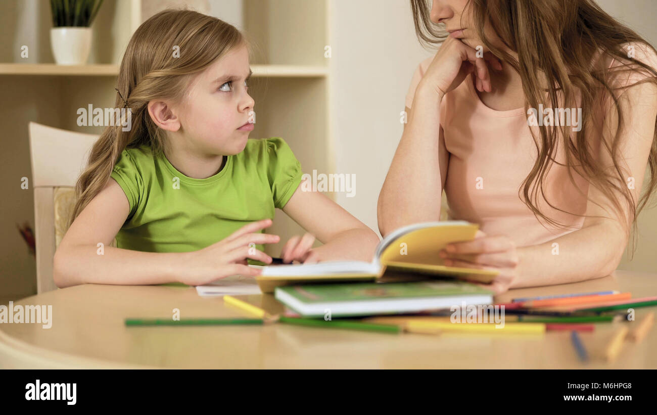 Upset little girl with misunderstanding looking at her mother doing ...