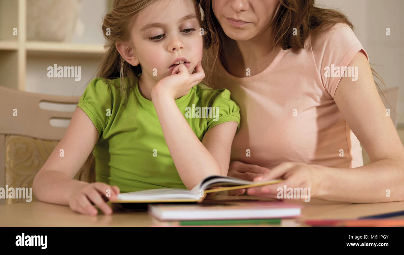 Supportive mother reading textbook together with hyperactive little ...