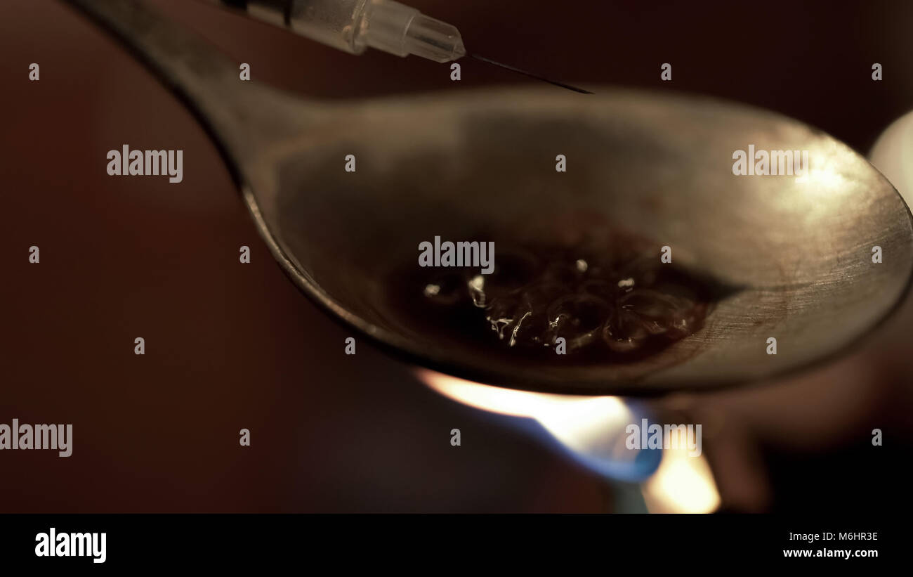 Close-up of liquid drug dose boiling in spoon, syringe needle prepared ...