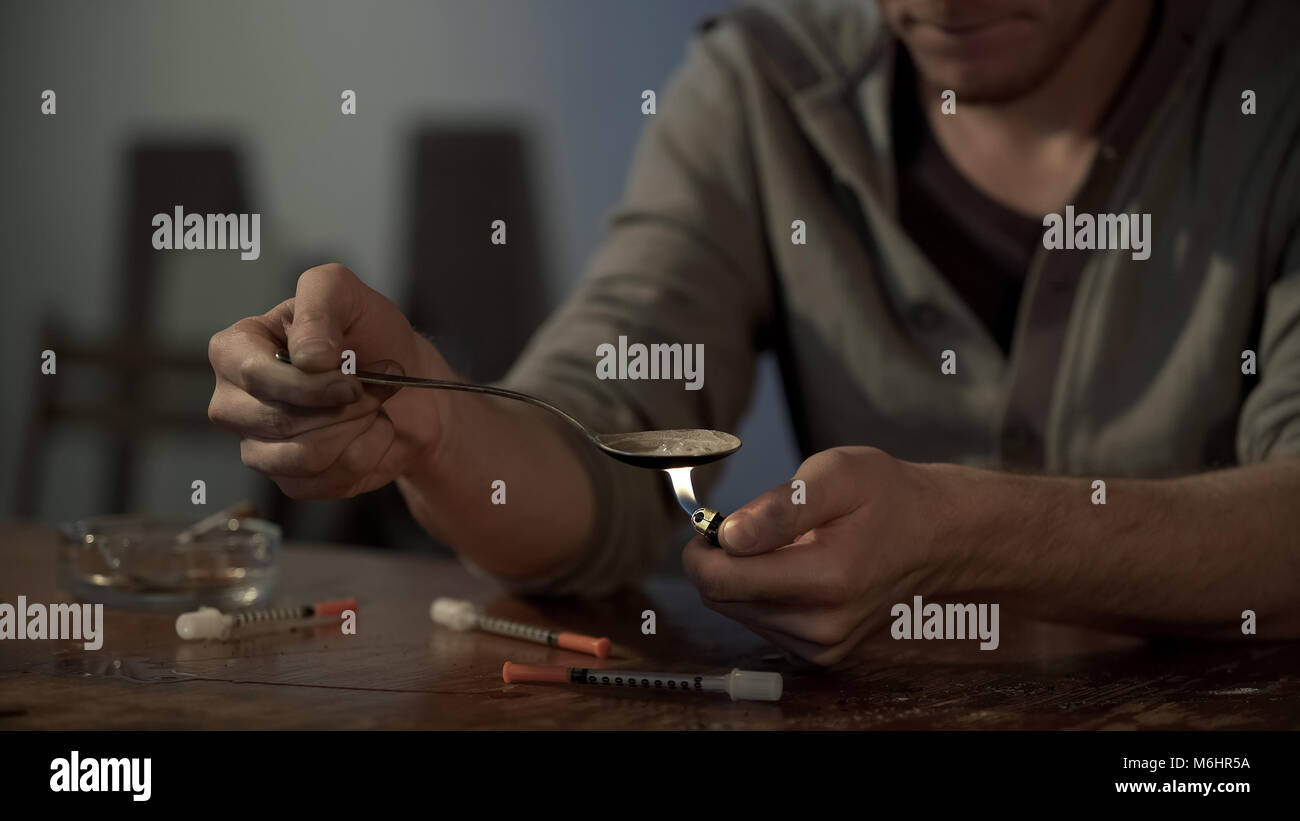 Addict preparing drug dose for injection, heating heroin on spoon ...