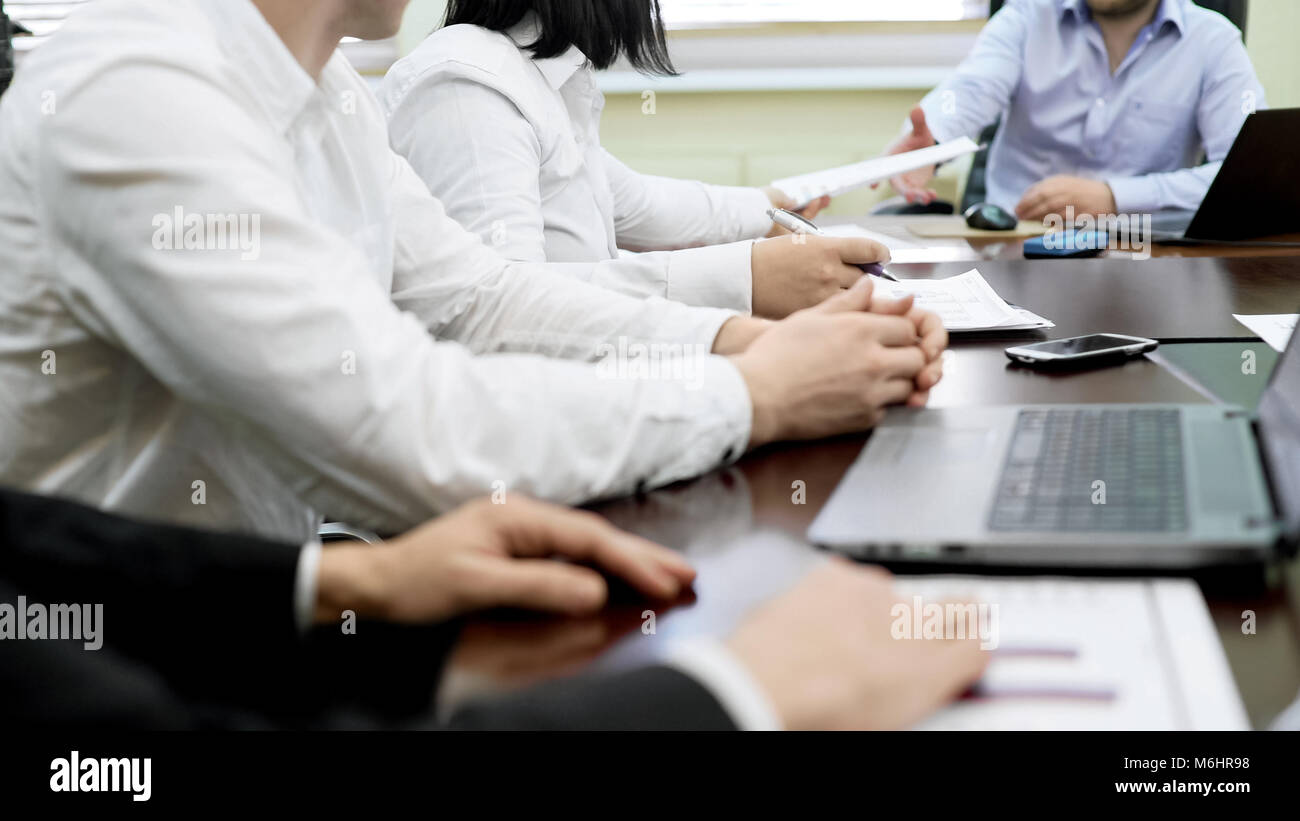 Company workers sitting at table at business meeting, listening to ...