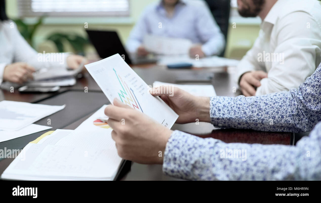 Managers sitting at table in meeting, looking at documents with data ...