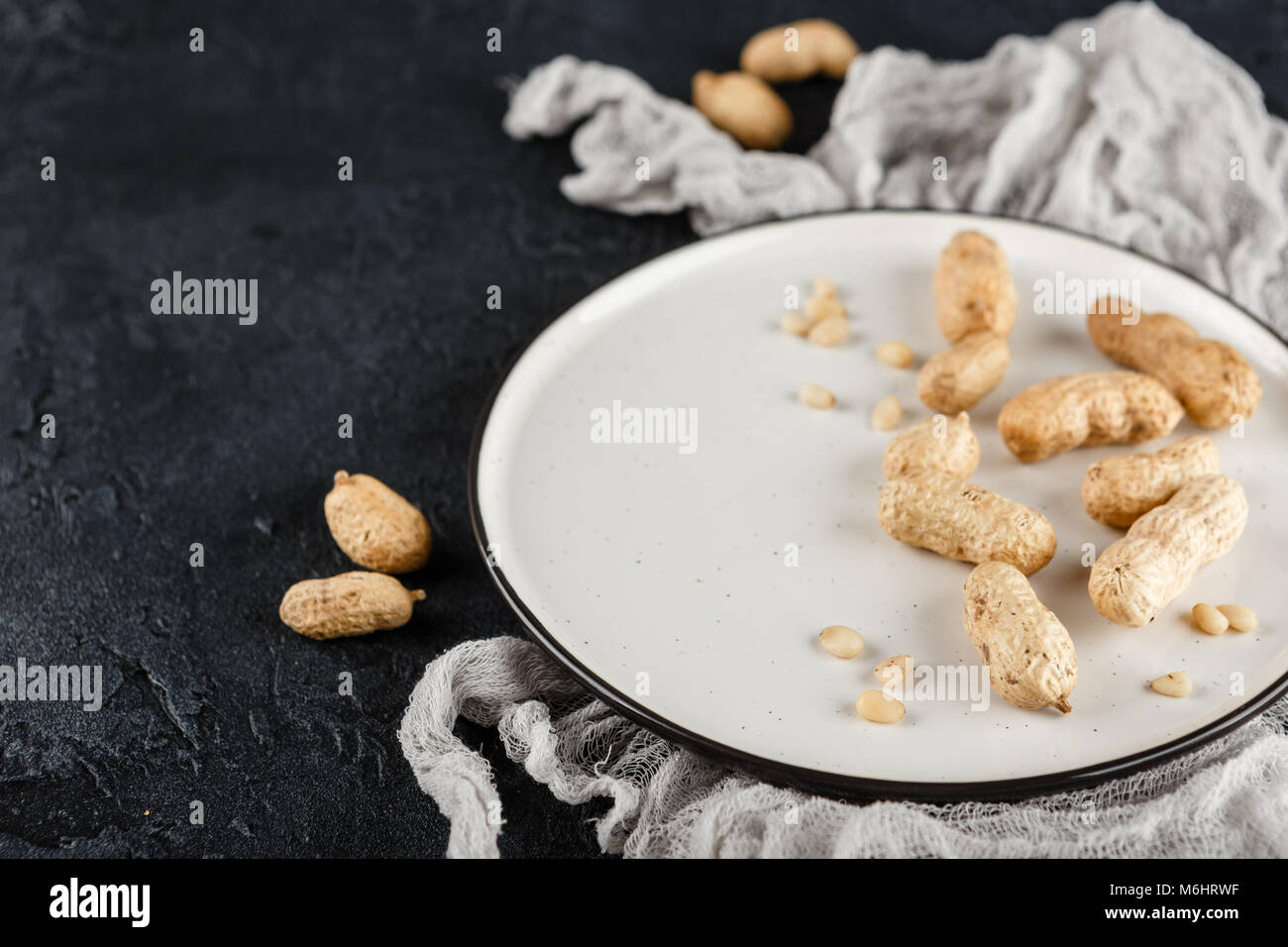 Peanuts in nutshell on a white plate with napkin on black background ...
