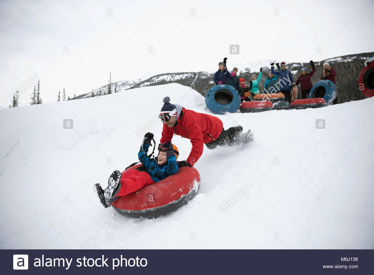 Family cheering father pushing son on inner tube in snow at tube park ...