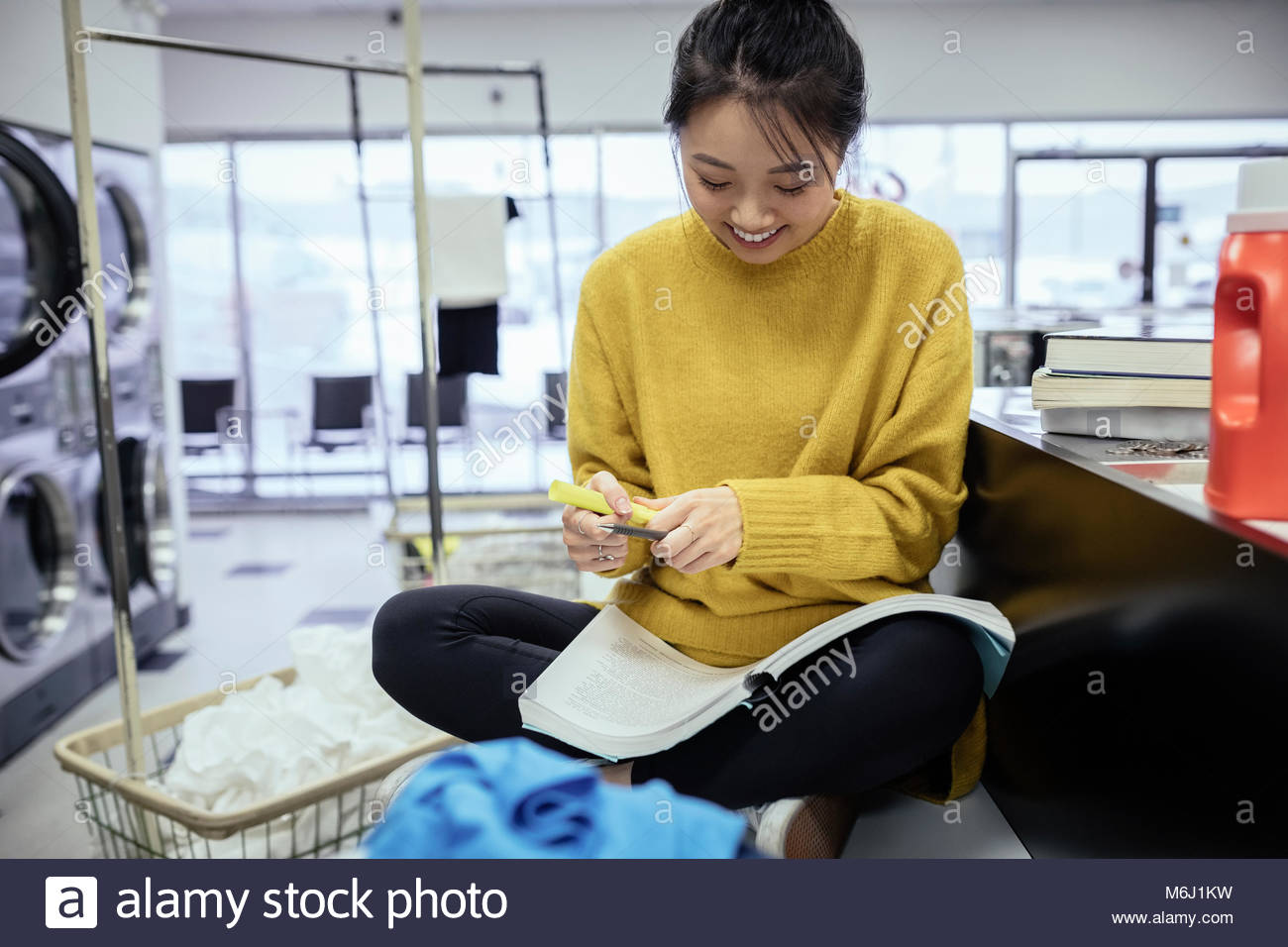 Female college student studying, waiting for laundry at laundromat ...