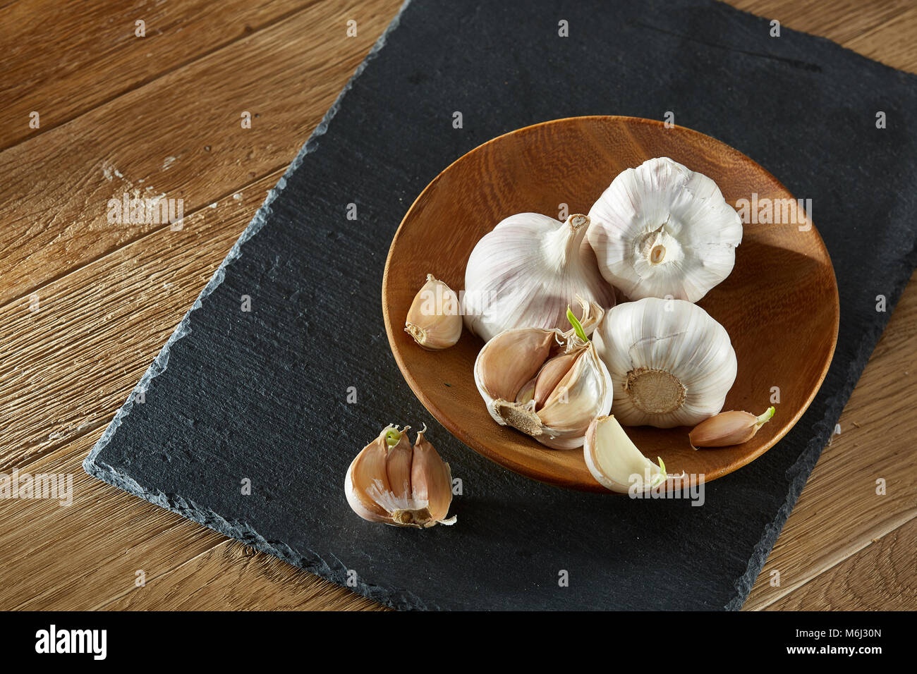 Garlic on flat wooden plate put on rustic rough wooden table with light ...