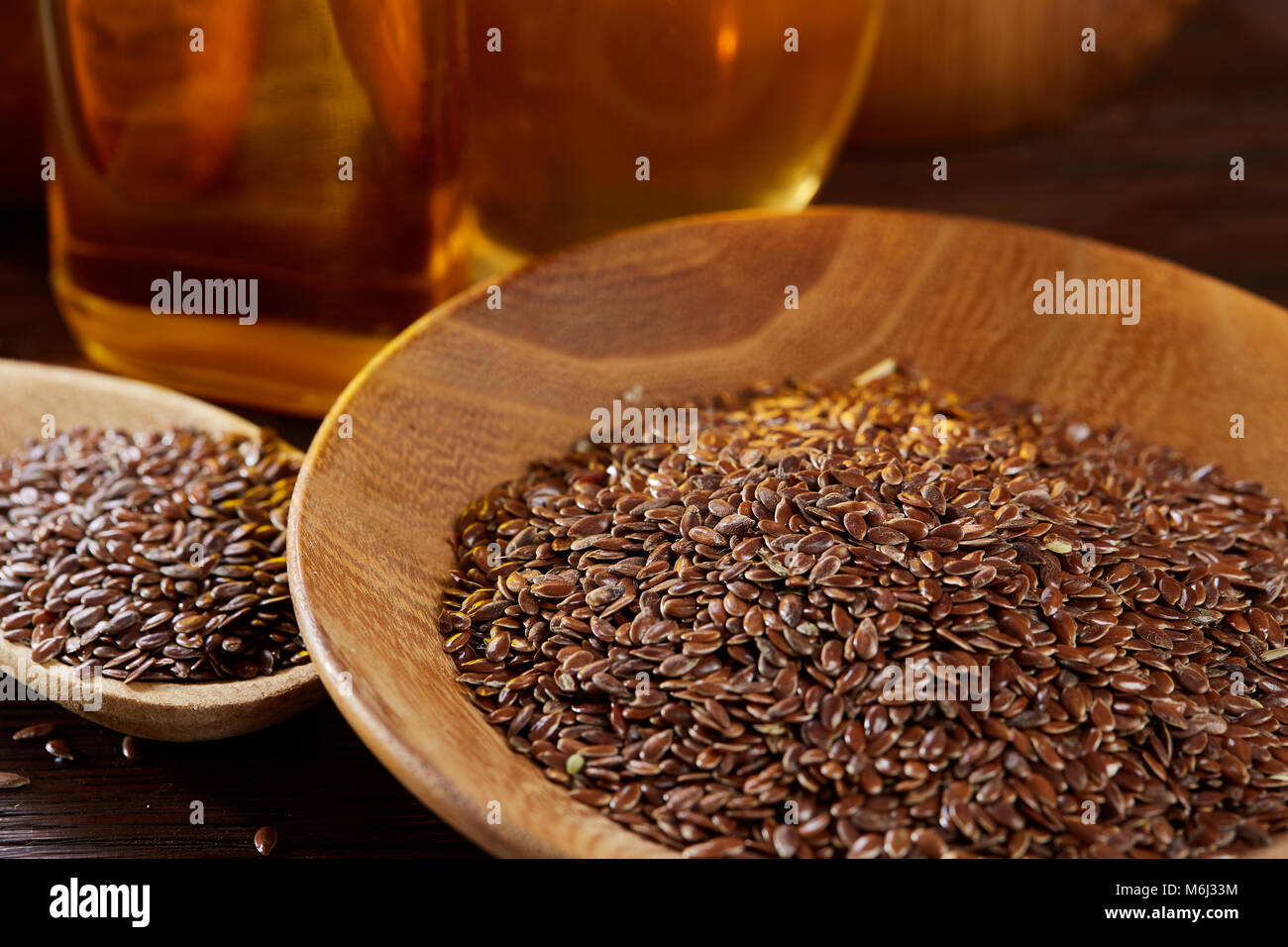 Brown flax seeds in wooden plate and flaxseed oil in glass bottle on brown rustic wooden ...